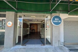 Entrada de hotel com porta de vidro, uma placa e um toldo metálico.