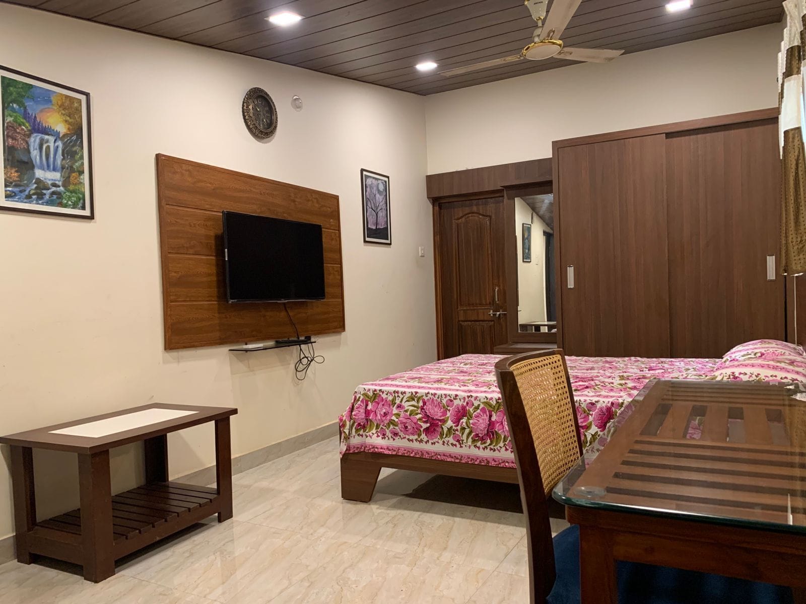 Quarto com cama, televisão na parede, guarda-roupa de madeira e uma mesinha.
