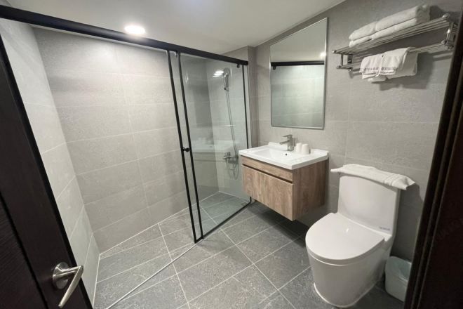 Uma casa de banho moderna com cabine de chuveiro em vidro, sanita branca, lavatório com espelho e porta-toalhas.