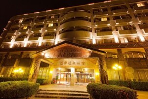 Um hotel de vários andares com entrada central, rodeado por sebes bem cuidadas.