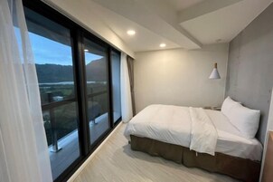 Quarto com uma janela grande, uma cama e uma luminária pendente.