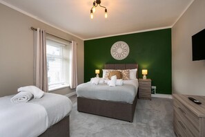 Quarto de hotel com uma cama, uma cama adicional, uma mesa de cabeceira com abajur, cômoda e televisão na parede.