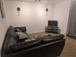 Uma sala de estar com um sofá de couro escuro, uma mesa lateral pequena e uma televisão de tela plana.