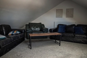 Uma sala de estar com um sofá de couro preto, uma mesa de centro de madeira e um radiador na parede.