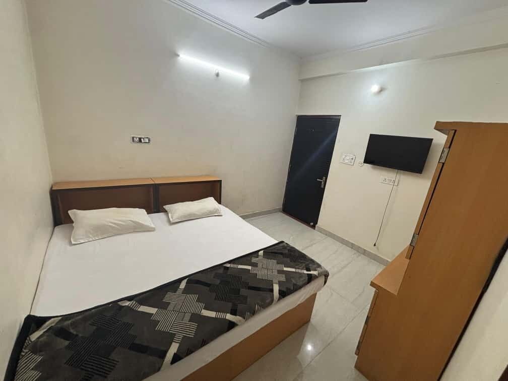 Um quarto com cama, ventilador de teto, televisão na parede e guarda-roupa.