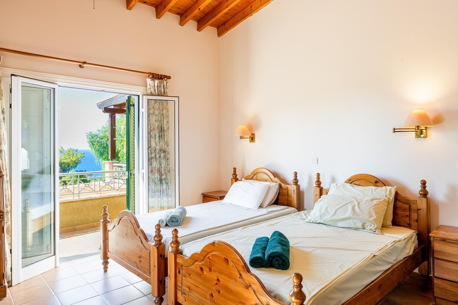 Quarto com cama de madeira, duas mesas de cabeceira, porta de vidro deslizante para área externa e duas luminárias fixadas na parede.