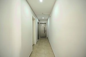 Um corredor estreito e bem iluminado com piso de azulejos, que leva a uma porta no final.