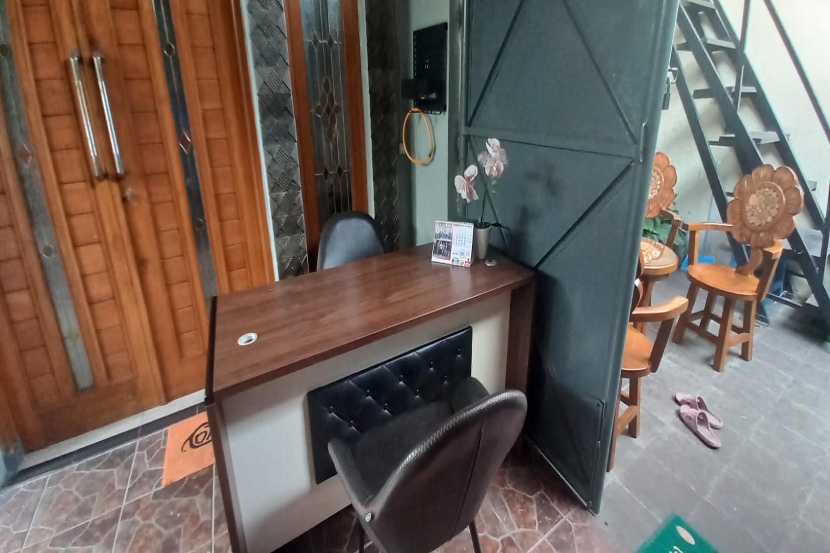 Uma receção com acabamento em madeira, uma cadeira estofada em preto e uma pequena planta em vaso.