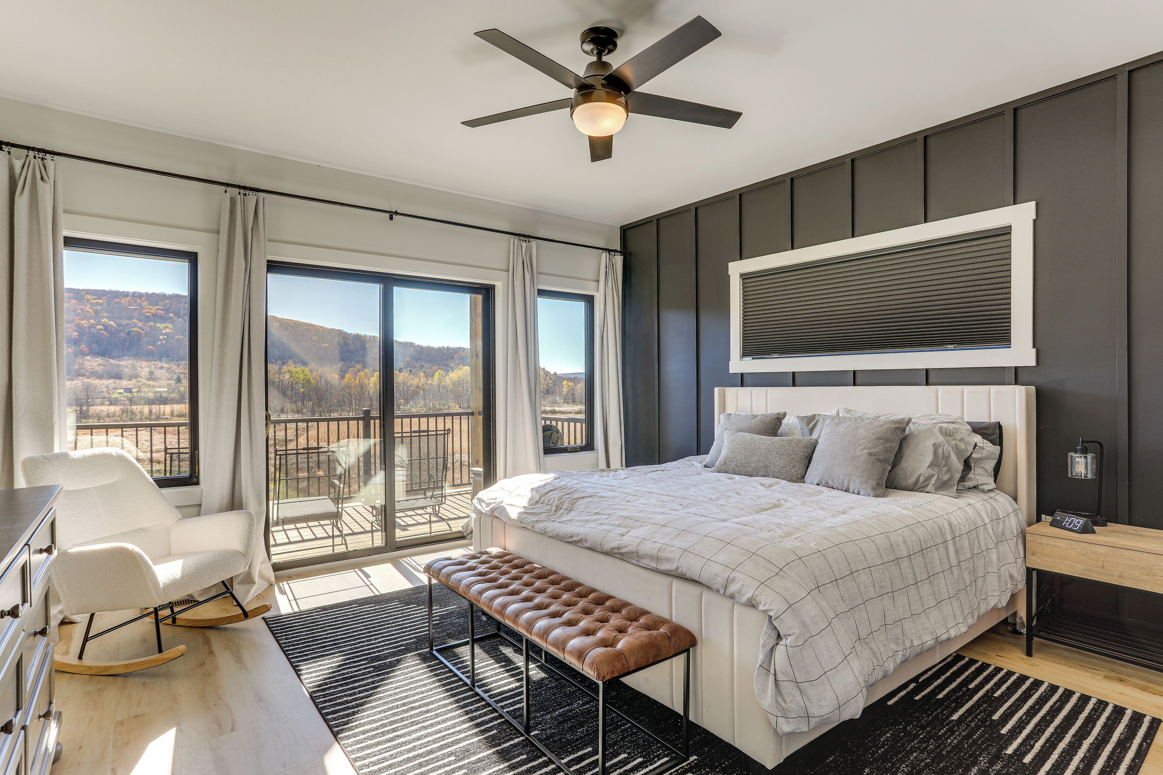 Quarto moderno com cama grande, um banco, uma escrivaninha e varanda com vista para as colinas.