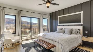 Quarto moderno com cama grande, um banco, uma escrivaninha e varanda com vista para as colinas.