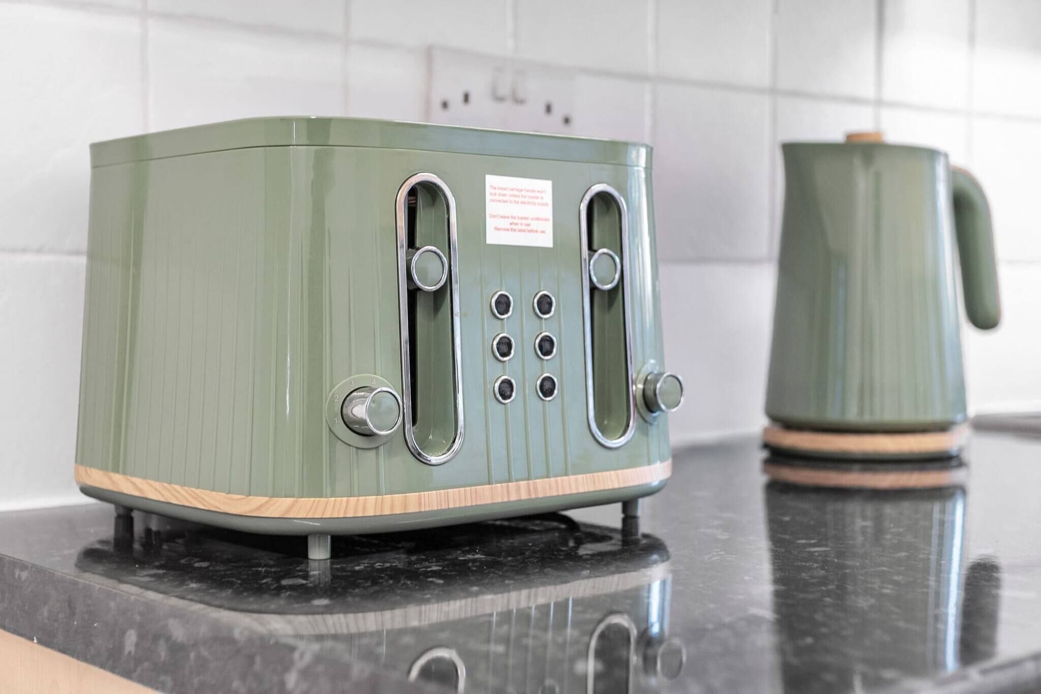 Uma torradeira de estilo retrô com base de madeira e corpo verde, sobre uma bancada preta em uma cozinha.