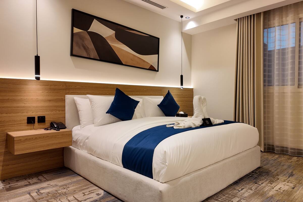 Quarto de hotel com uma cama grande, cabeceira de madeira, mesa de cabeceira com telefone e um quadro na parede.