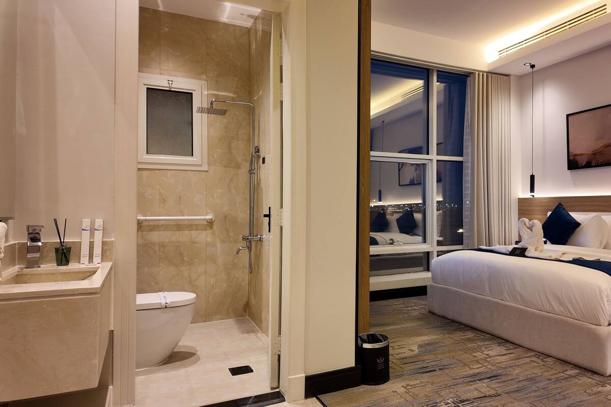 Quarto de hotel com banheiro, cama e uma grande janela com vista.