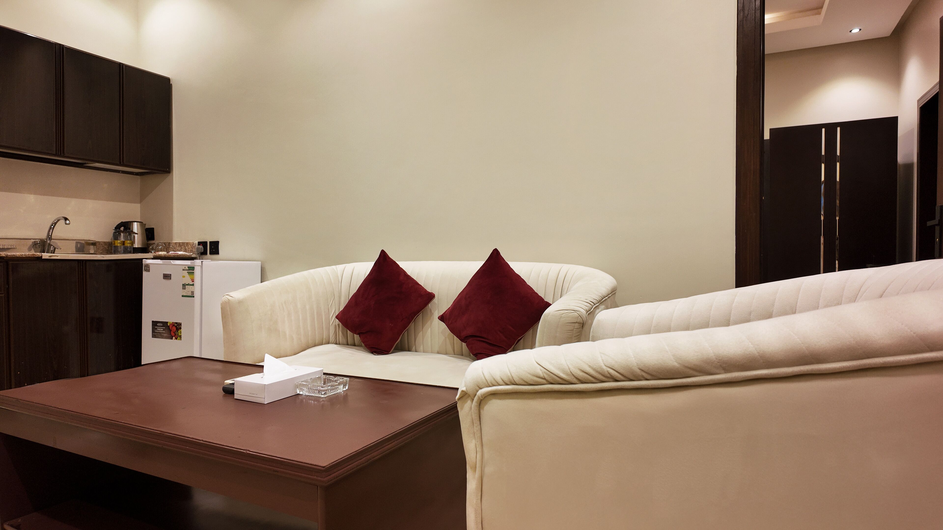Quarto de hotel com cozinha compacta, sofá com duas almofadas, mesa de centro e uma cama.