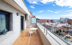 Uma varanda com piso de azulejos, duas cadeiras brancas e uma mesa.