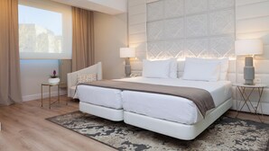 Quarto de hotel moderno com uma cama grande, duas mesas de cabeceira, uma cabeceira decorativa e vista para a cidade pela janela.