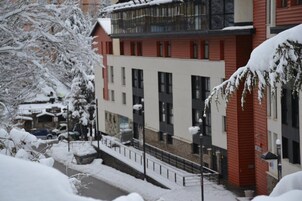Edifício de vários andares com fachada vermelha e pisos superiores brancos, cercado por árvores cobertas de neve e uma calçada.