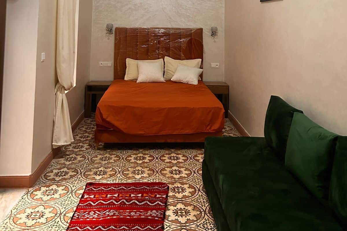 Quarto com cama, sofá verde, carpete estampado e um quadro na parede.