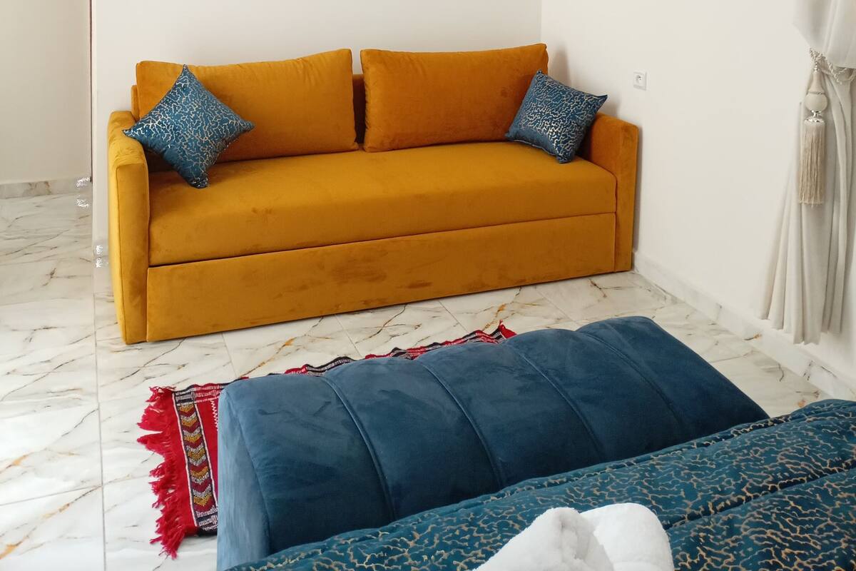 Uma sala de estar com um sofá amarelo-mostarda, um sofá azul, uma TV de tela plana e um quadro colorido na parede.