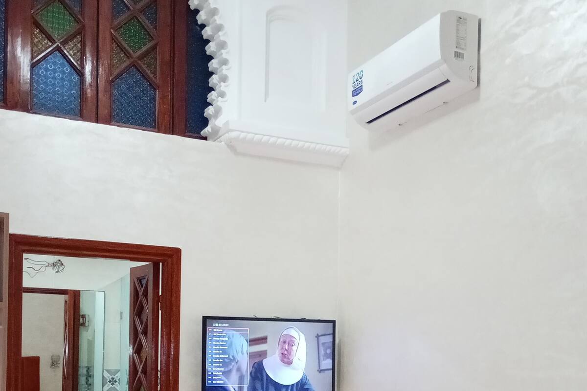 Casa de banho com televisão na parede, uma prateleira de madeira e um aparelho de ar condicionado.