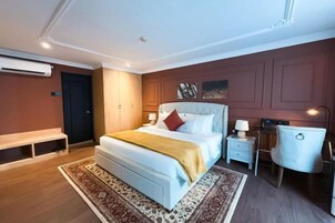 Quarto com uma cama grande, mesas de cabeceira, uma cadeira e uma escrivaninha.