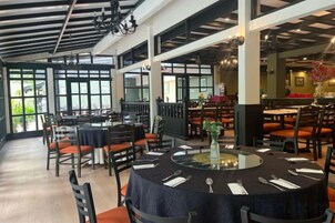 Um restaurante com mesas redondas, cadeiras e uma mesa com tampo de vidro.