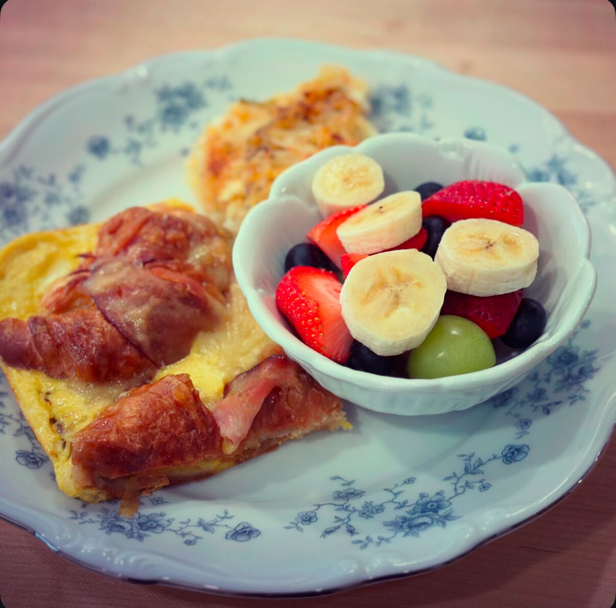 Um prato com uma fatia de omelete de fiambre e queijo, e uma tigela com frutos vermelhos e uvas.