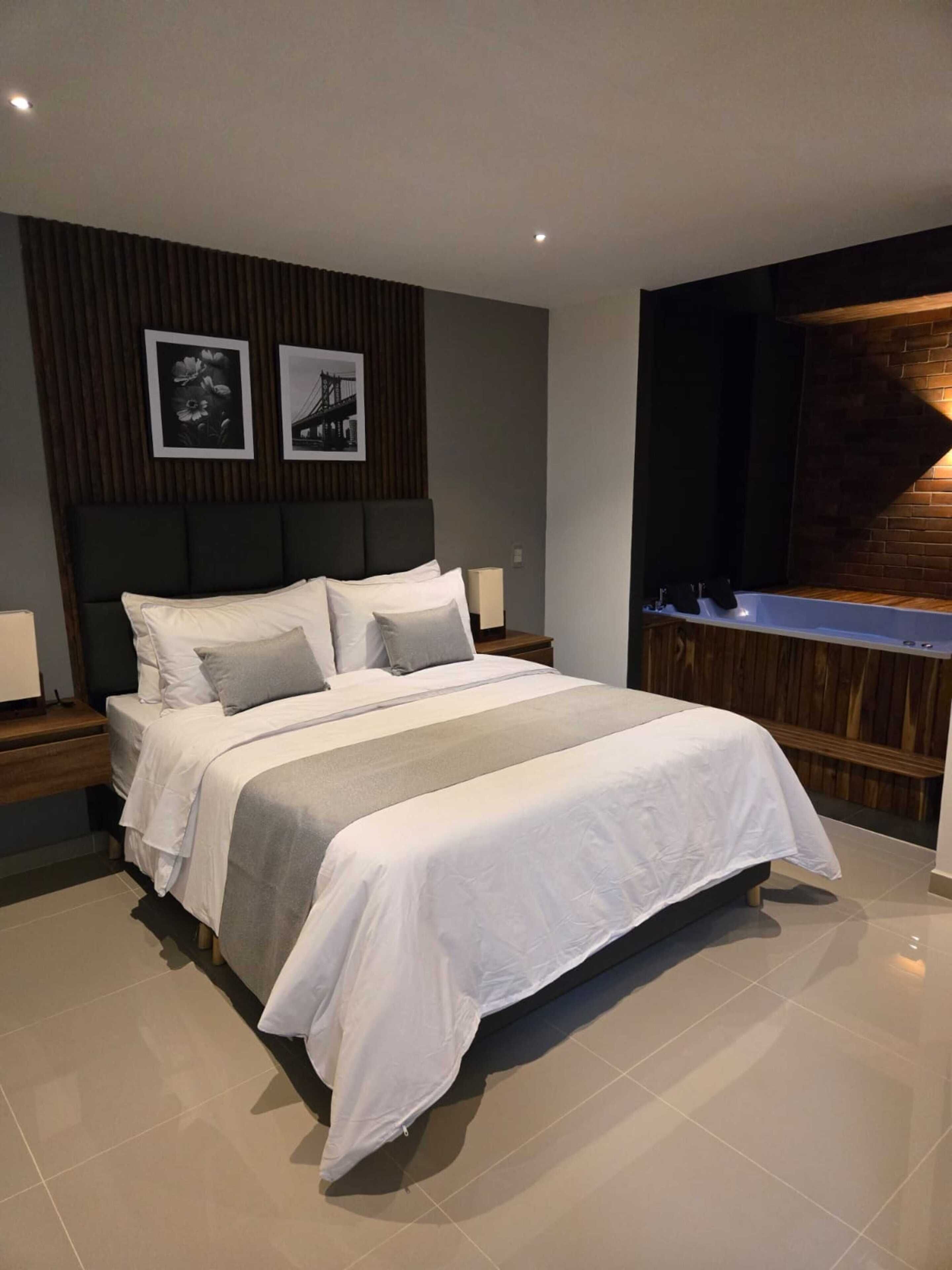 Quarto moderno com uma cama grande, uma mesinha de cabeceira, televisão fixada na parede e uma banheira integrada.