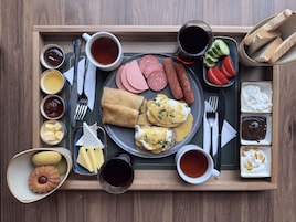 Uma bandeja com itens de café da manhã, como ovos, salsichas, presunto e torradas, juntamente com acompanhamentos e bebidas.