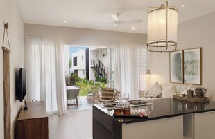 Uma sala de estar moderna com uma ilha central, televisão de tela plana na parede e área de jantar com vista para o exterior.