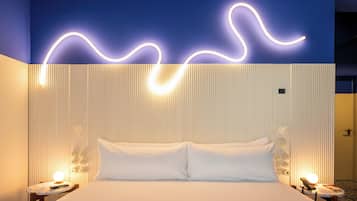 Quarto de hotel com cama, mesas de cabeceira, luminária na parede e uma porta.