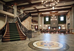 Um hall amplo com uma escadaria imponente, uma lareira de pedra e um grande candelabro.