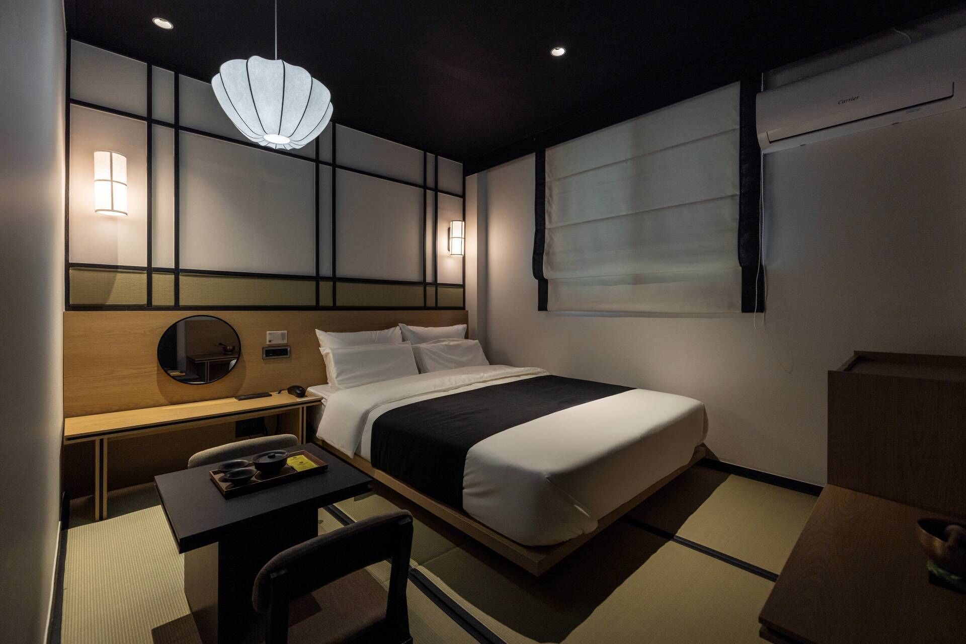 Quarto de hotel moderno com cama, mesa de cabeceira e escrivaninha com cadeira.