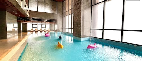 Piscina interna com água cristalina, grandes janelas e uma placa indicando um hotel de luxo.