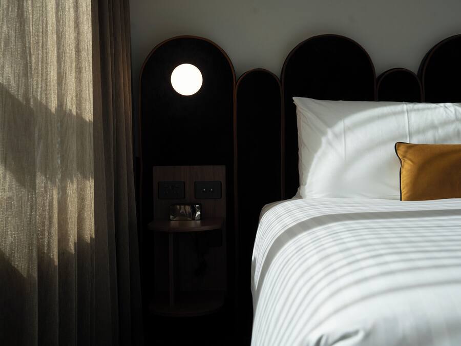Quarto de hotel com cama, mesa de cabeceira e luminária na parede.