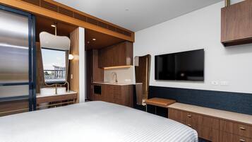 Quarto de hotel moderno com uma cama grande, banheiro com pia e espelho, e televisão fixada na parede.