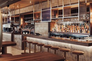 Uma área de bar com balcão, banquetas e prateleiras repletas de garrafas e copos.