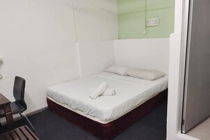 Quarto pequeno com uma cama de solteiro, uma cadeira de madeira, uma escrivaninha e parede verde.
