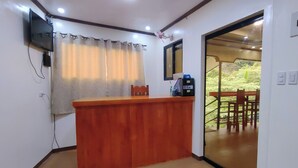 Quarto com uma mesa de recepção de madeira, televisão montada na parede e uma janela com cortina.