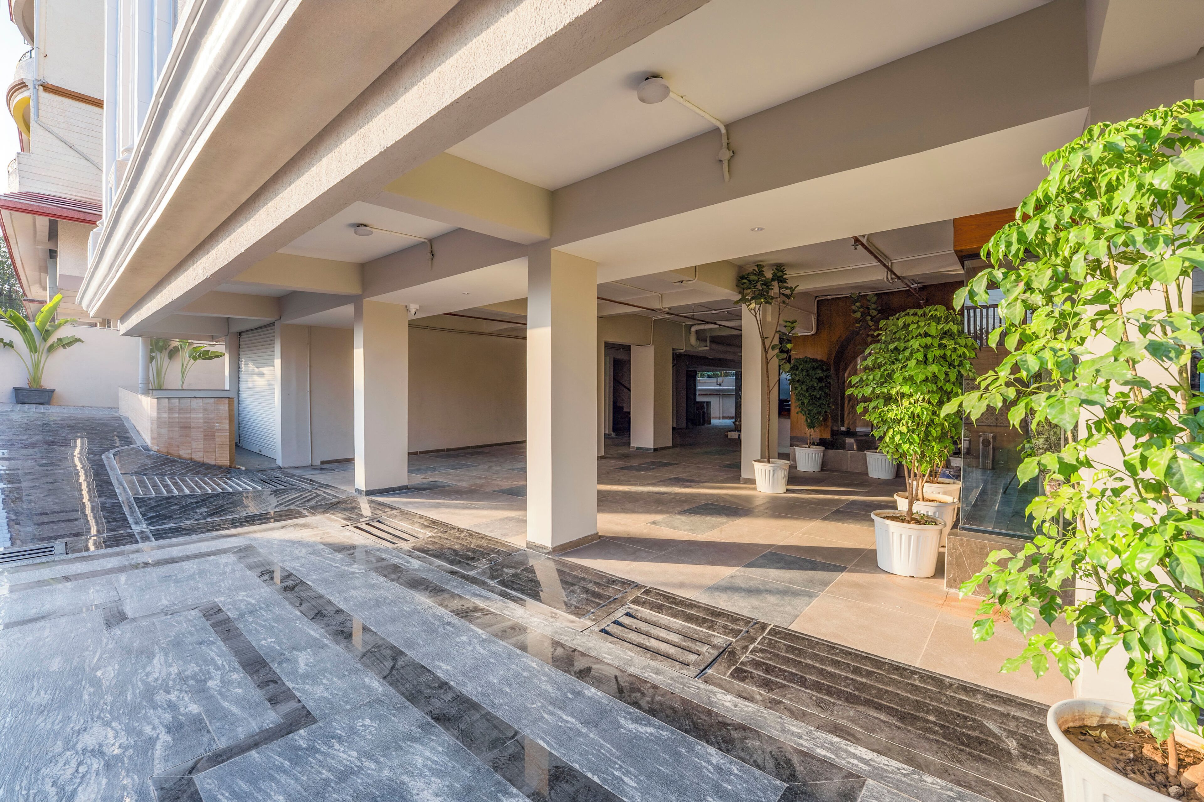 Amplo espaço ao ar livre com piso de azulejos, plantas em vasos e vista desobstruída para o interior do edifício.
