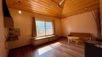 Quarto com piso de madeira, ventilador de teto, janela com cortinas, sofá e uma mesa.