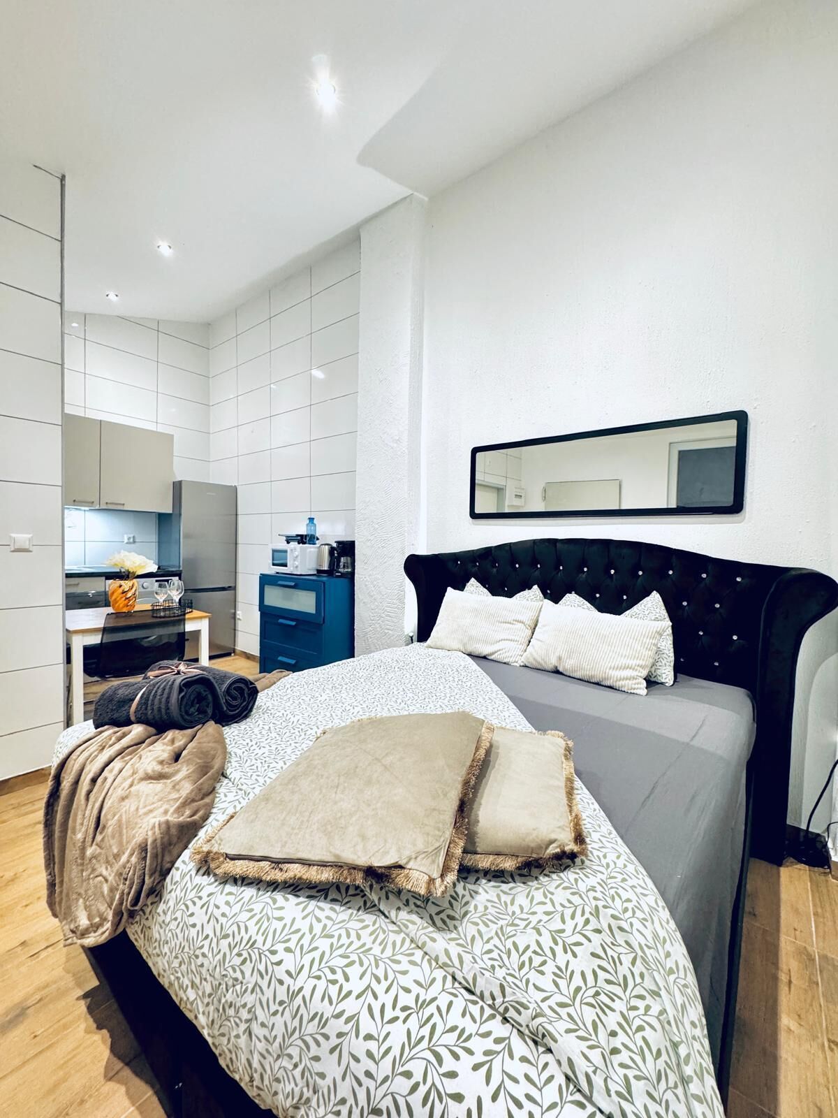 Quarto moderno com cama grande, mesa de cabeceira, espelho e vista para cozinha.