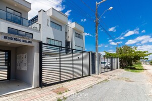 Um edifício residencial moderno com entrada protegida por grades, painel elétrico visível e céu claro.