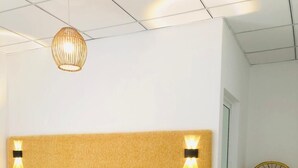 Quarto de hotel com uma cama grande, cabeceira com luzes acopladas à parede, luminária pendente e uma pequena prateleira com objetos.