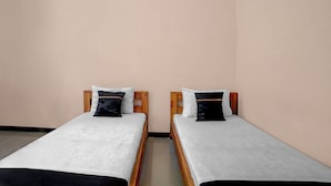 Duas camas de solteiro com cabeceiras de madeira e roupa de cama branca, em um quarto com paredes lisas e chão de azulejos.