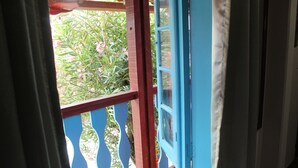 Uma porta aberta com vista para uma varanda com guarda-corrimão azul e uma planta com flores cor-de-rosa.