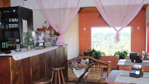 Uma área de bar com geladeira repleta de bebidas, uma pequena árvore de Natal e um espaço de estar com um banco de madeira e banquetas.