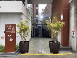 Entrada de um edifício com uma placa indicando 'MOBI ONE PAULISTA' e duas plantas em vasos.
