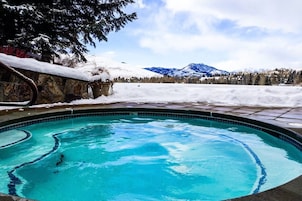 Uma piscina com água azul cristalina, rodeada por terreno coberto de neve e montanhas ao fundo.