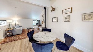 Ampla sala de estar com uma mesa redonda de mármore e cadeiras azuis, um sofá e uma mesinha de centro.